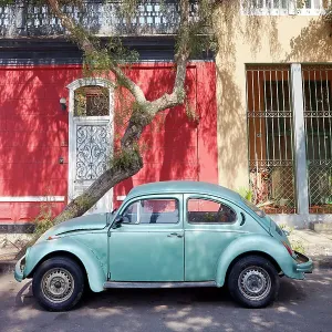A vintage Volkswagen beetle car in front of a colonial